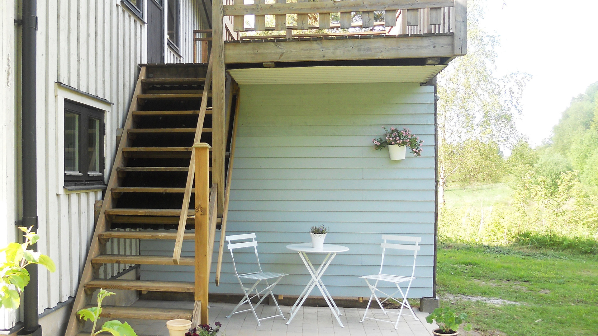 En uteplats vid ett blått hus med en trapp upp till en balkong.