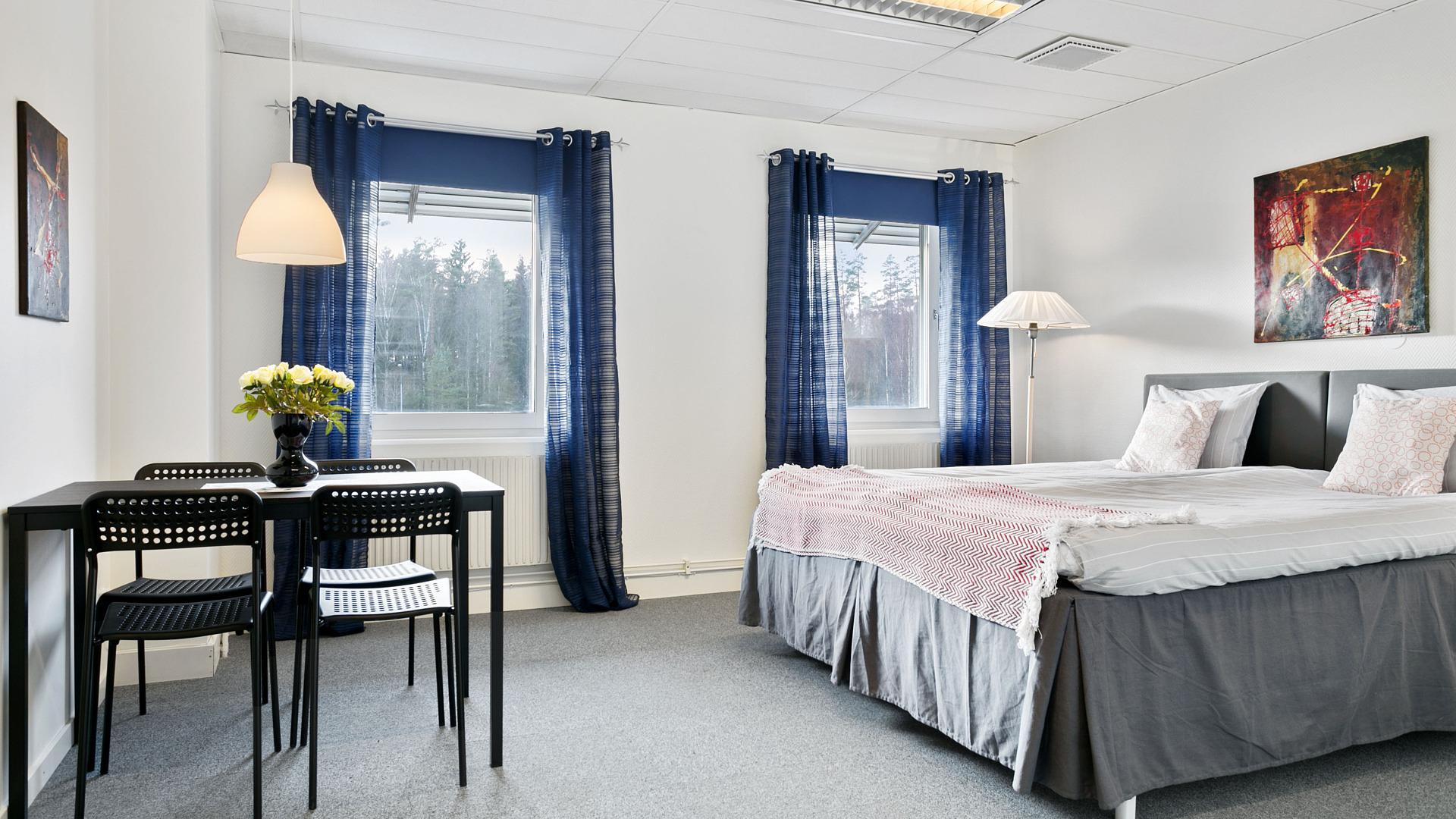 Hotellrum i grått med dubbelsäng och bord och stolar.