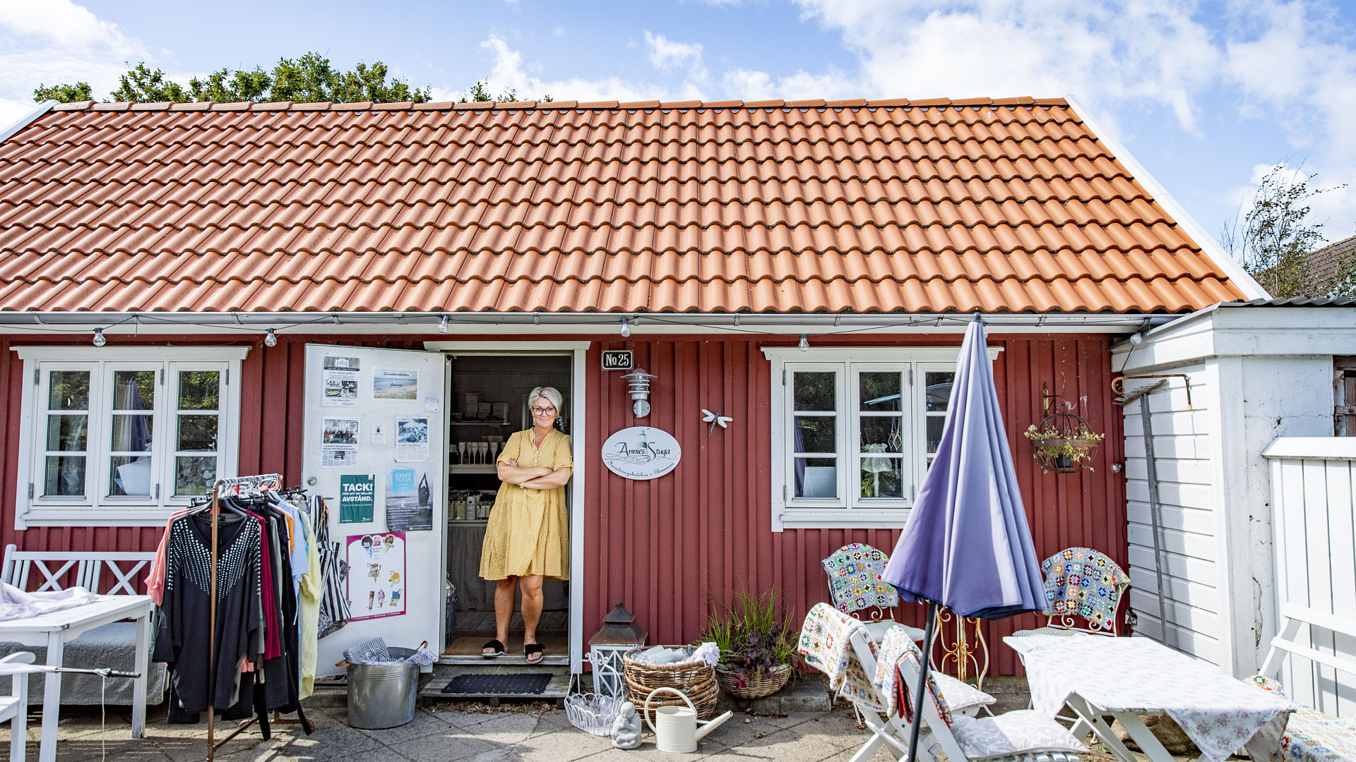 Kvinna står i dörröppningen till ett rött hus och inredningsbutik.