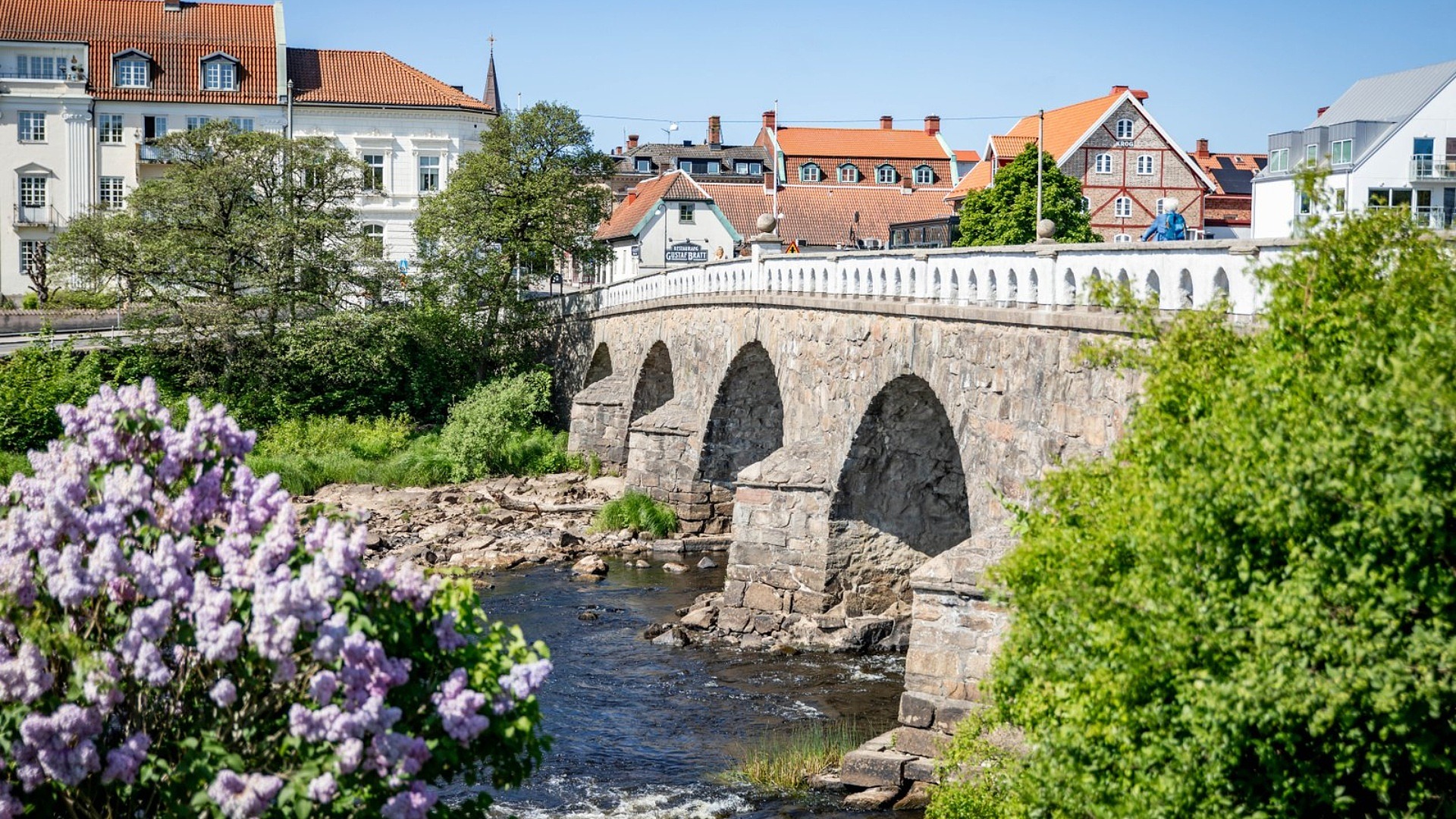 Stenbro omgivet av grönska och gamla hus.